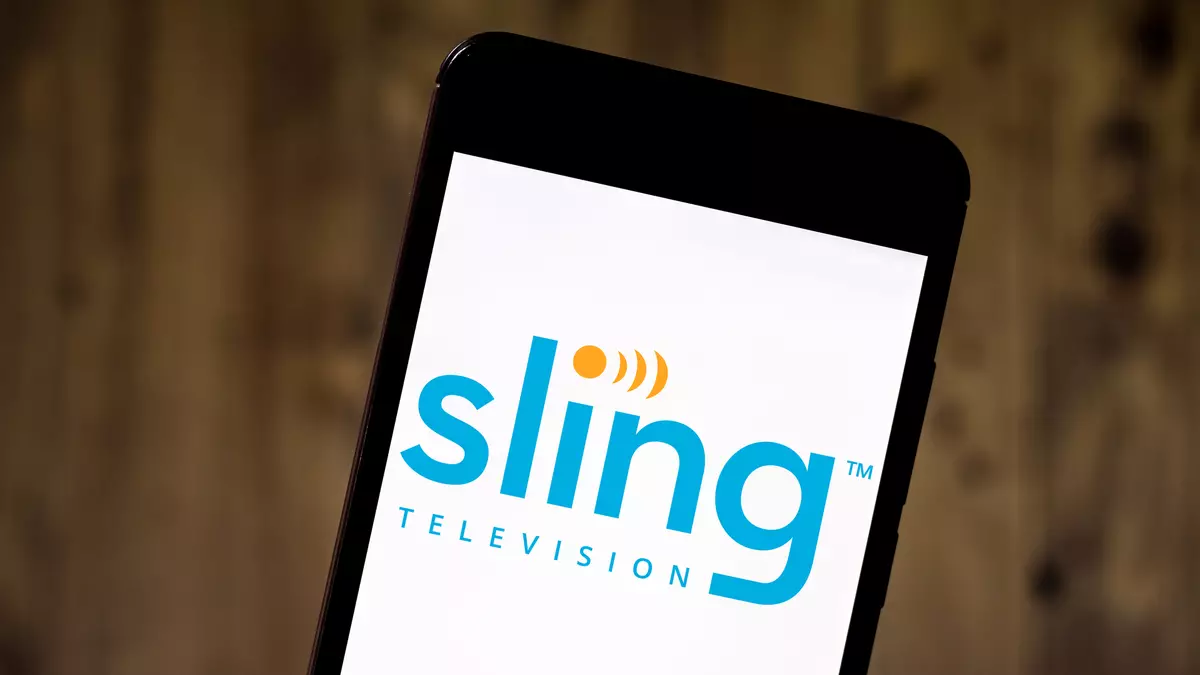 Лагатып SLING TV адлюстроўваецца на смартфоне перад драўляным фонам