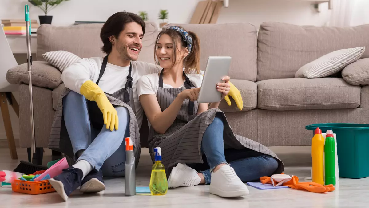 Χαρούμενο νεαρό ζευγάρι που σταματά από τον καθαρισμό για να χρησιμοποιήσει μια εφαρμογή σε ένα tablet
