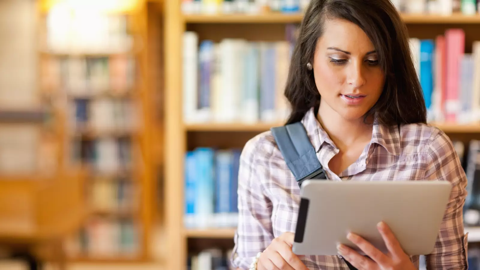 Коллежийн номын санд таблет ашиглан анхаарлаа төвлөрүүлж буй залуу оюутан