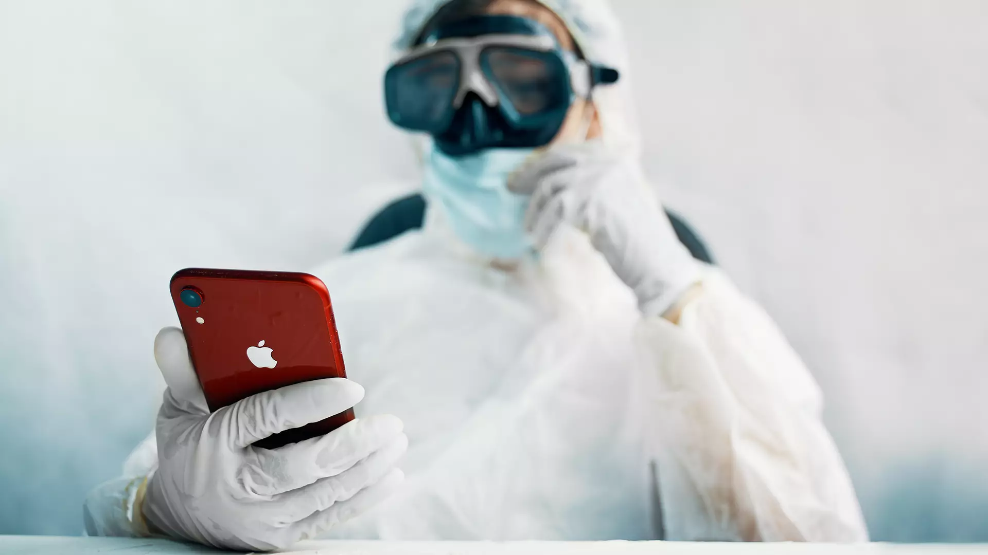 Uma pessoa em um traje de risco biológico tentando desbloquear seu iPhone.