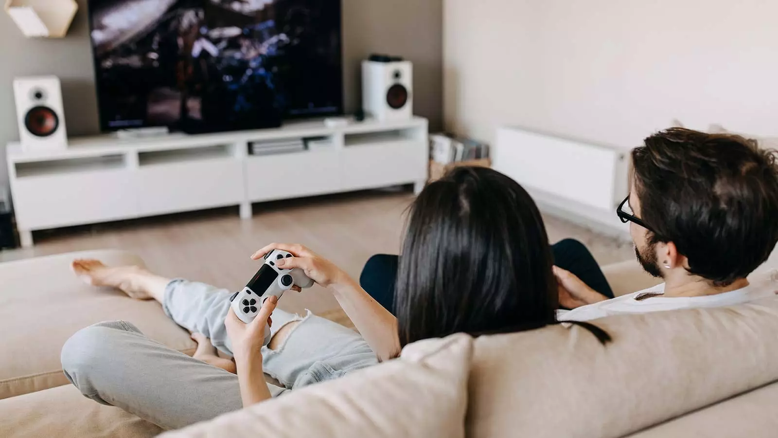 Para wylegująca się na kanapie, grająca razem w grę wideo.