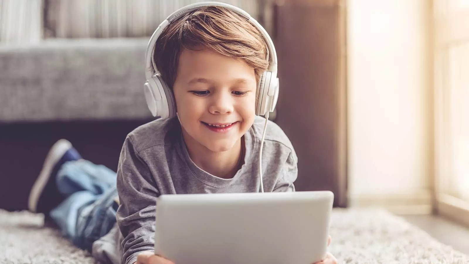 En dreng, der lytter til hovedtelefoner, mens han bruger en tablet i en solrig stue.