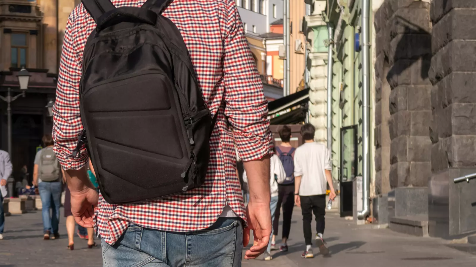 Siyah bir sırt çantası takan bir şehir caddesinde yürüyen kişi