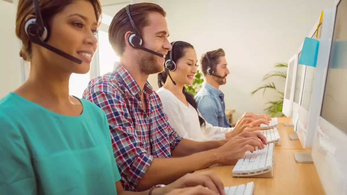 Nhóm dịch vụ khách hàng doanh nghiệp làm việc cùng nhau tại trung tâm cuộc gọi đeo tai nghe gõ máy tính