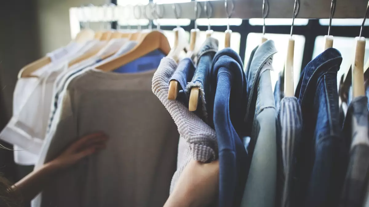 Kadın elleriyle bir raftaki kıyafetleri sıralayan giyim mağazası