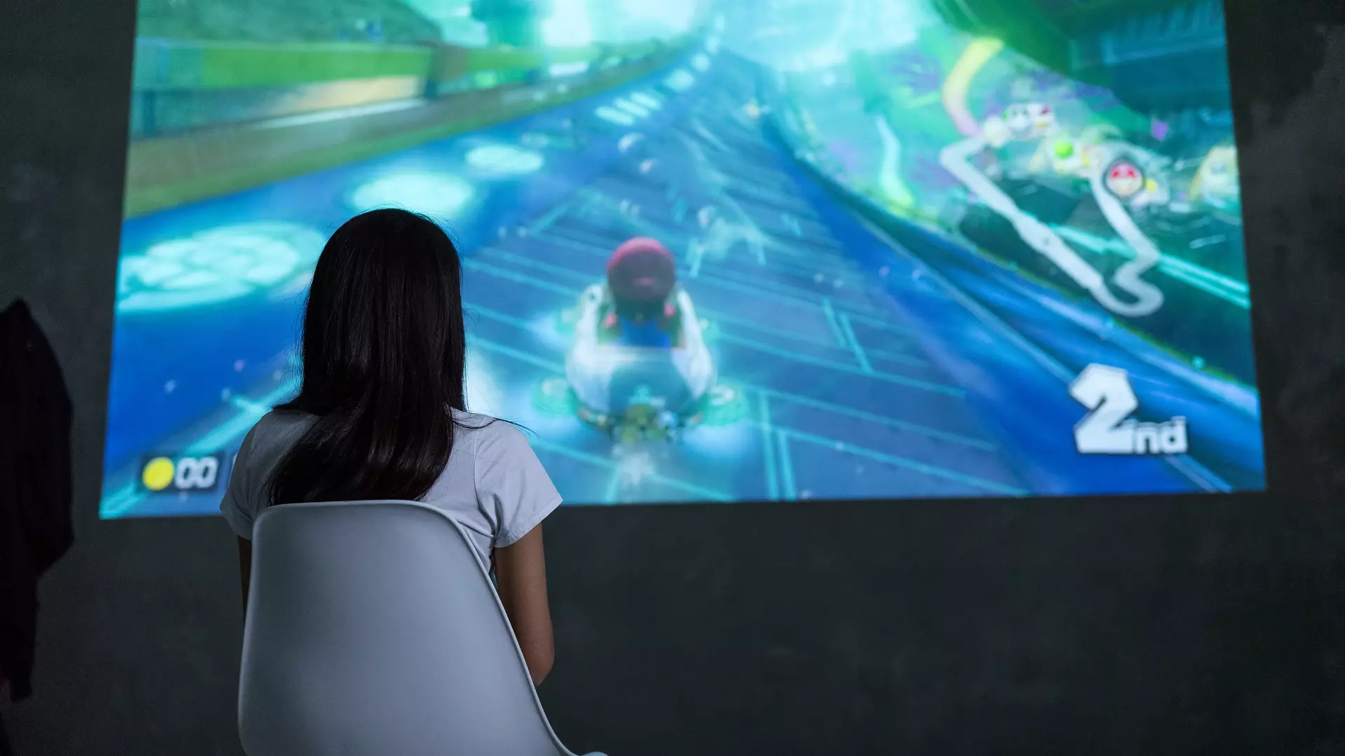 Uma mulher jogando Mario Kart em uma tela projetada