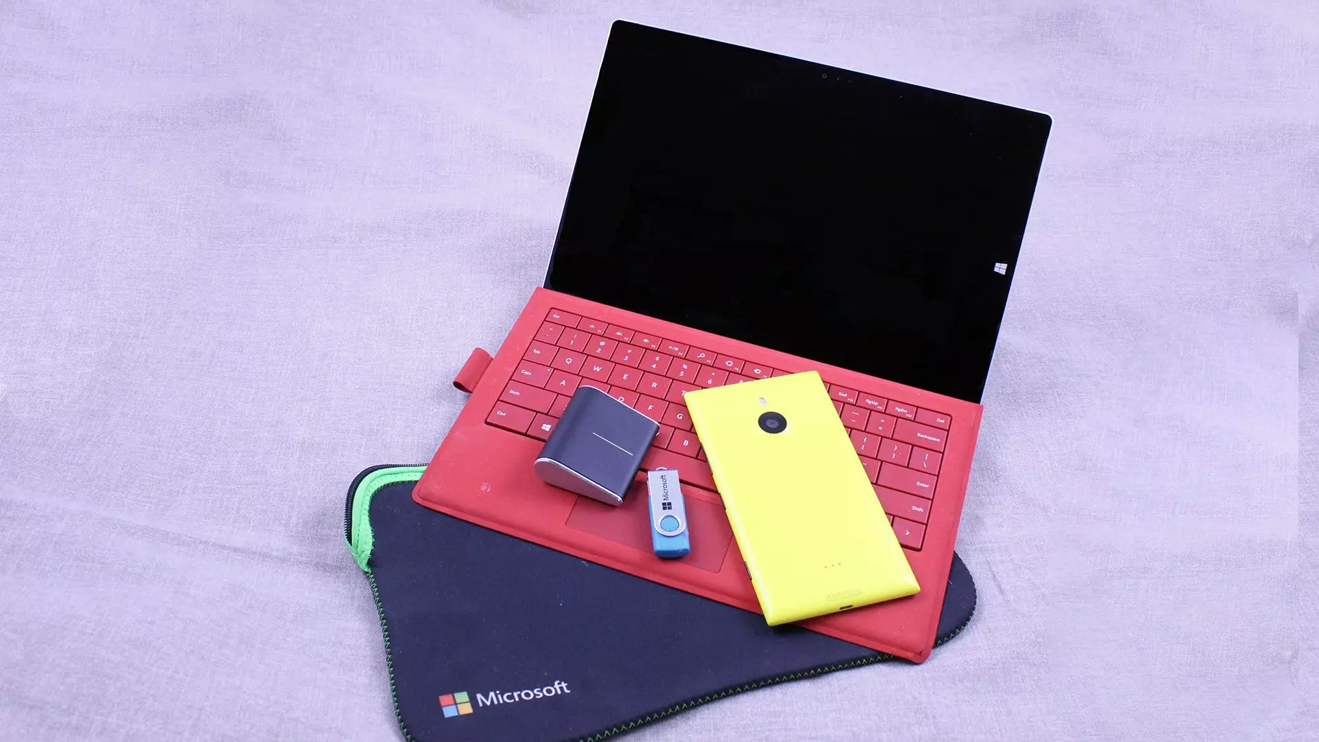 Microsoft Surface Pro 3, žlutý telefon s Windows, myš Surface Mouse a značkové pouzdro a telefon.