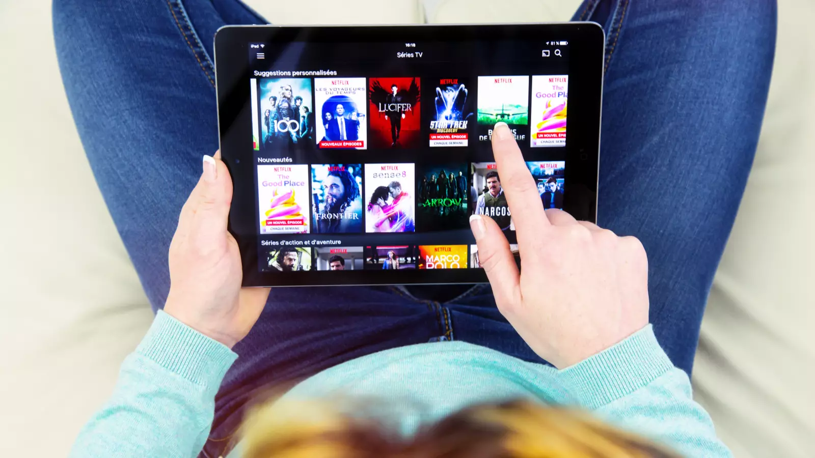 Žena sedí so skríženými nohami na gauči a pomocou tabletu sleduje filmy online
