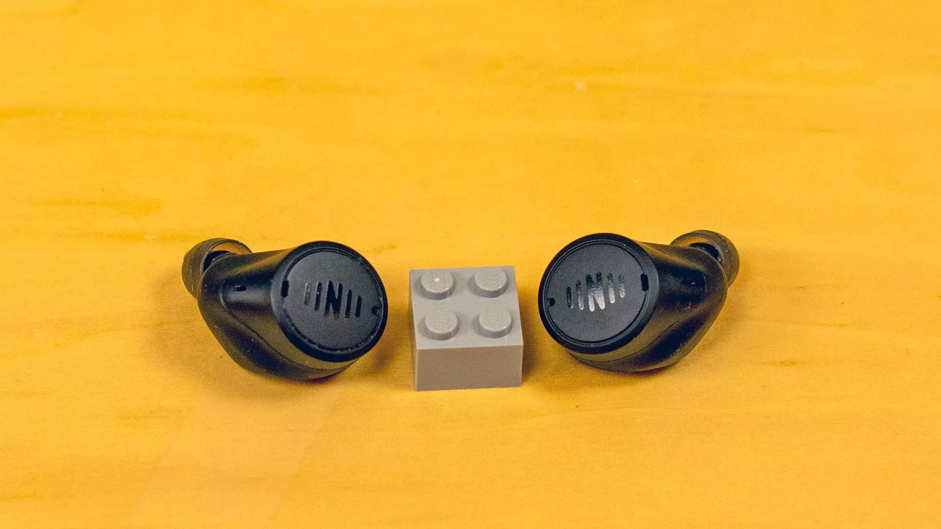 Un conjunt d'auriculars Nuheara IQbuds 2 Max al costat d'un maó LEGO 4x4 de la mateixa mida.