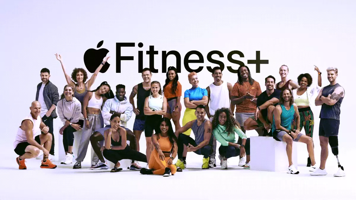 Liela grupa trenažieru stāv priekšā Apple Fitness+ logotipam