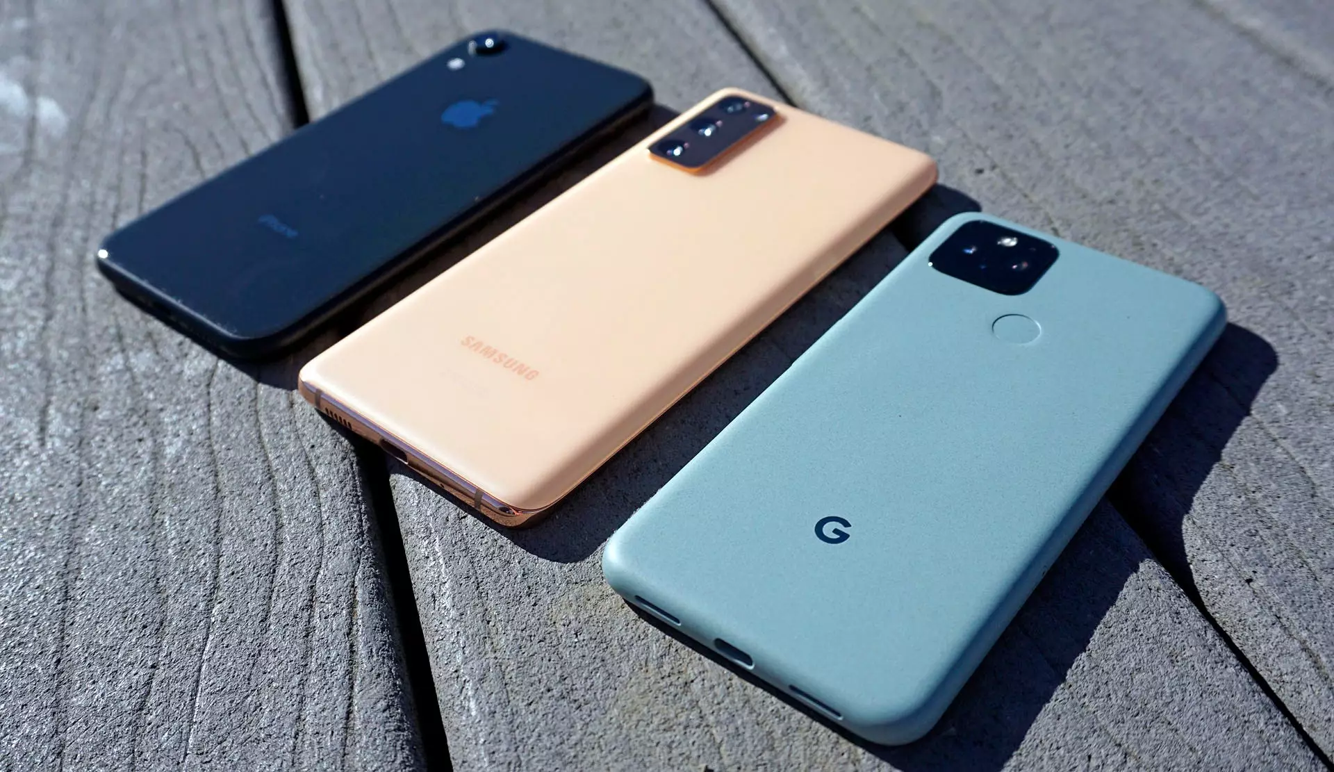 Komparante grandecon: iPhone XR, Galaxy S20 FE kaj Pixel 5, en vico sur ligno
