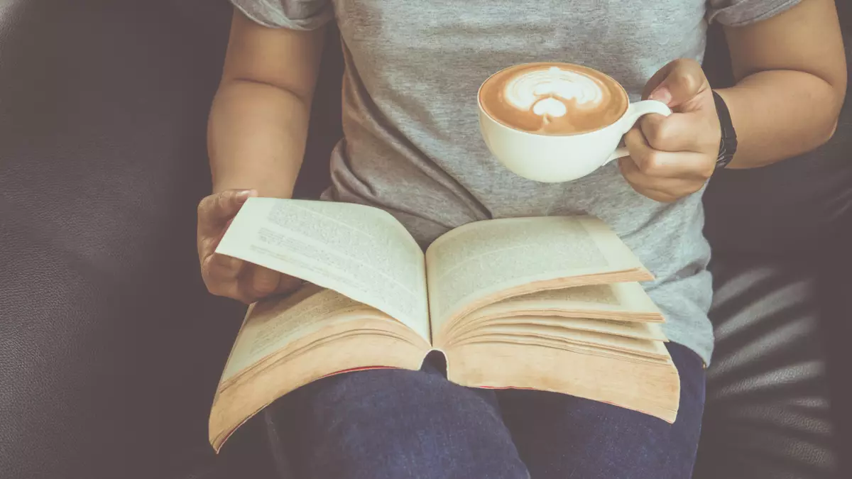 Nuori nainen lukee kirjaa ja kädessään kuppi kahvia