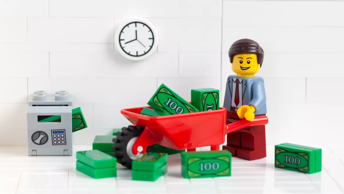 Minifigurka podnikatele Lego převážející peníze na kolečku.
