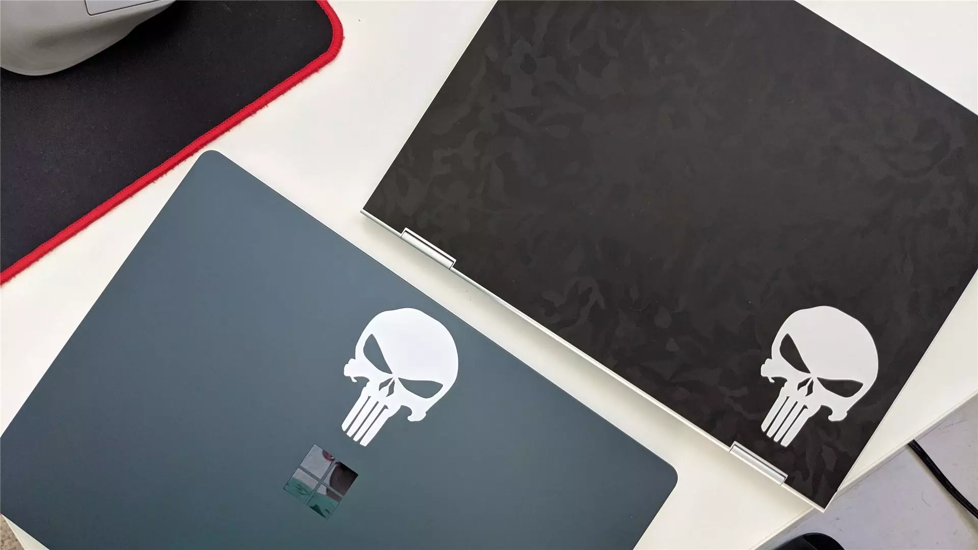 El Pixelbook con una funda de camuflaje negra y una laptop Surface 3, ambos con calcomanías de Punisher