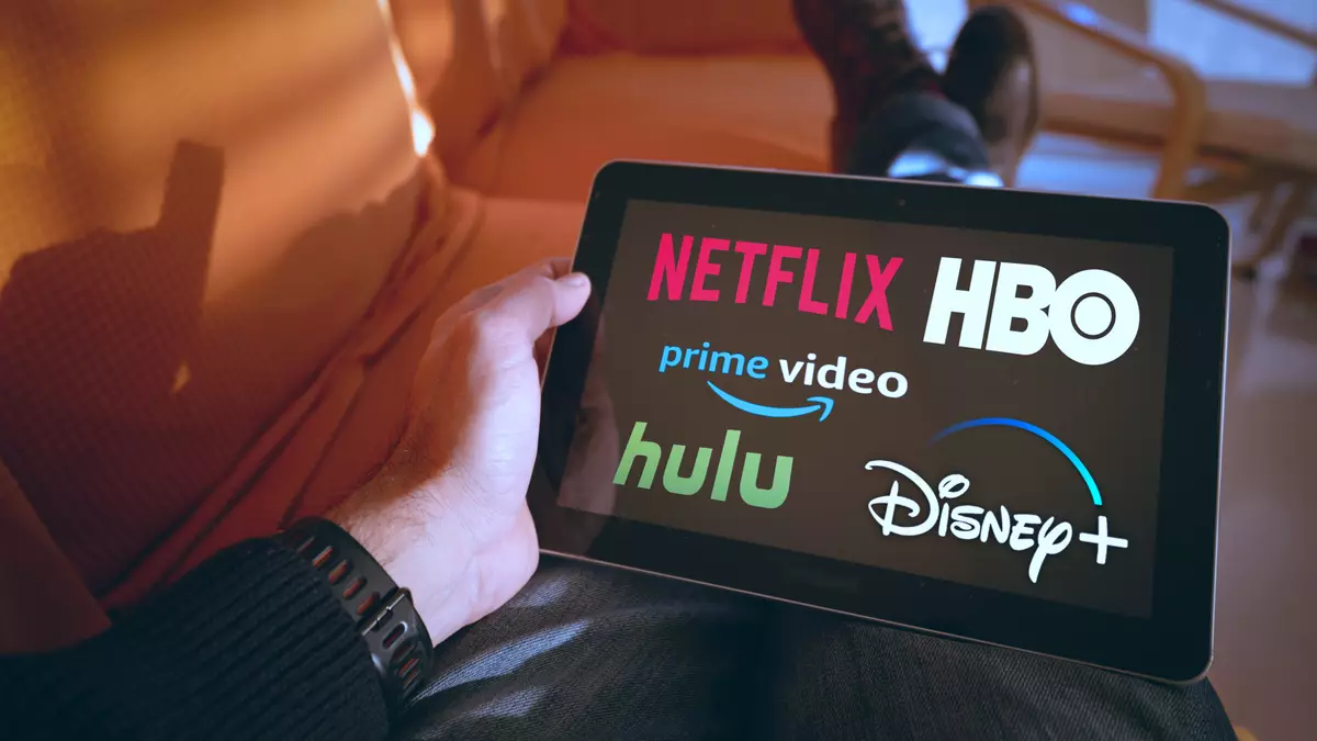 De Mann hält en Tablet mat Netflix, Hulu, Amazon Video, HBO, an Disney + Logoen