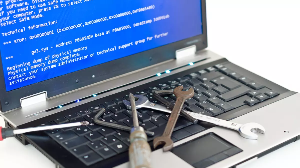 Komputer riba dengan ralat skrin biru dan alatan pada papan kekunci.