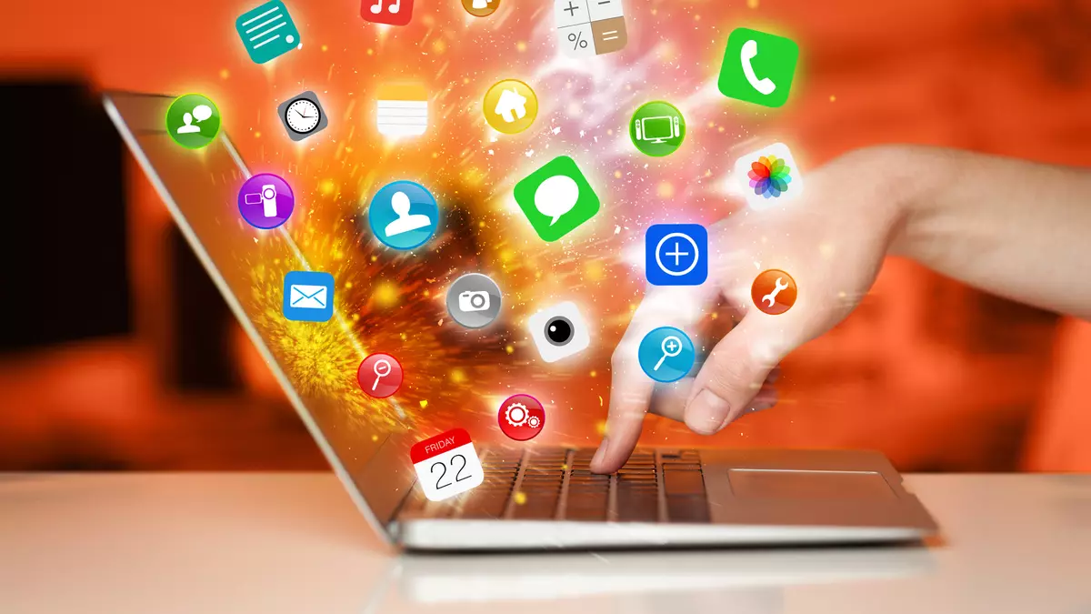 Tangan menekan laptop modern dengan ikon dan simbol aplikasi seluler keluar