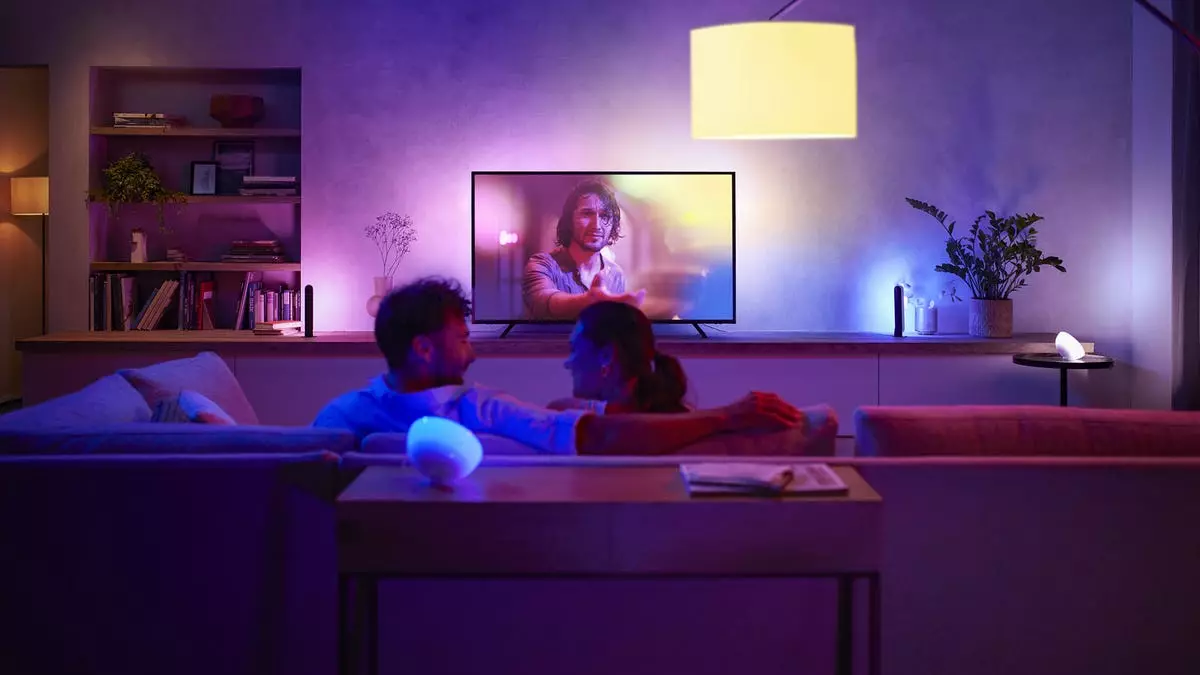 Philips Hue लाइट्सने वेढलेल्या लिव्हिंग रूममध्ये एक जोडपे टीव्ही पाहत आहे