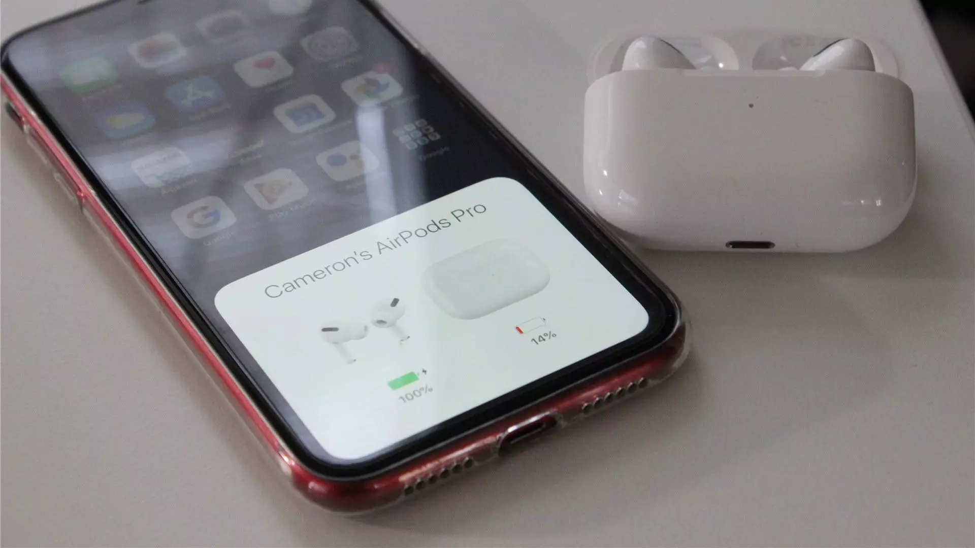 AirPods Pro هڪ iPhone XR جي اڳيان کليل آهي بيٽري اسٽيٽس اسڪرين ڏيکاريندي