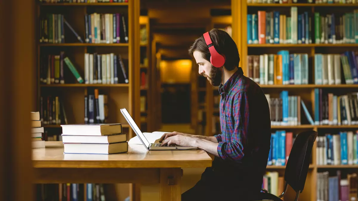 Um homem usando fones de ouvido com um laptop em uma biblioteca