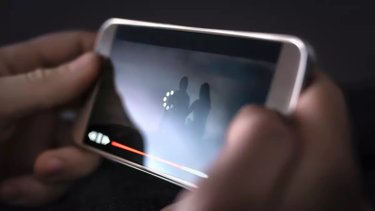 Человек, держащий телефон, со значком загрузки над потоковым видео.