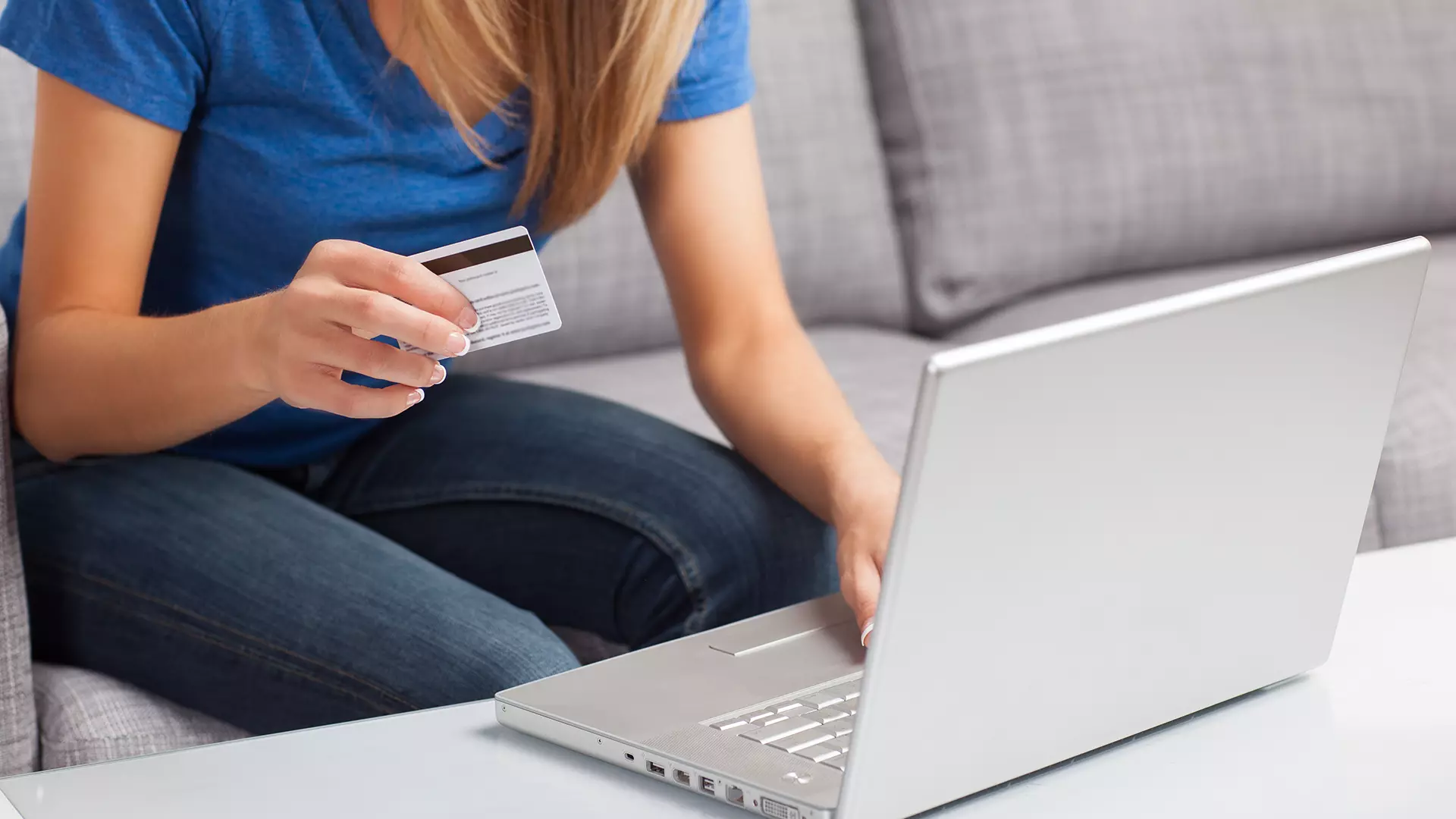 Egy nő keze egy kártyát tart, míg a másik keze egy laptop billentyűzetén.
