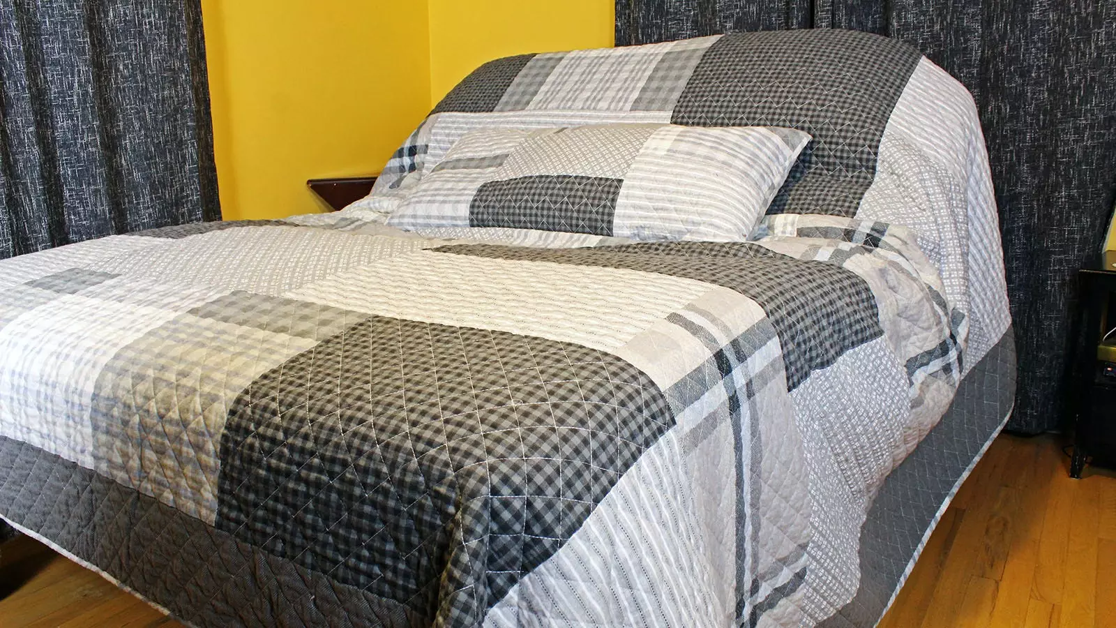 Sebuah katil dengan kaki dan kepala terangkat, ditutup dengan selimut kelabu dan putih.