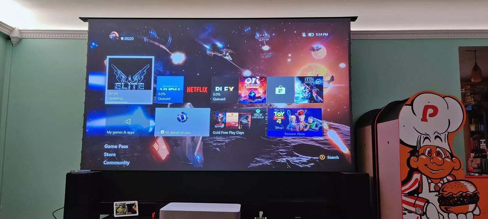 Гэрэлтүүлэг сайтай өрөөнд Xbox-ын үндсэн дэлгэцийг харуулсан 100 инчийн аварга том дэлгэц.