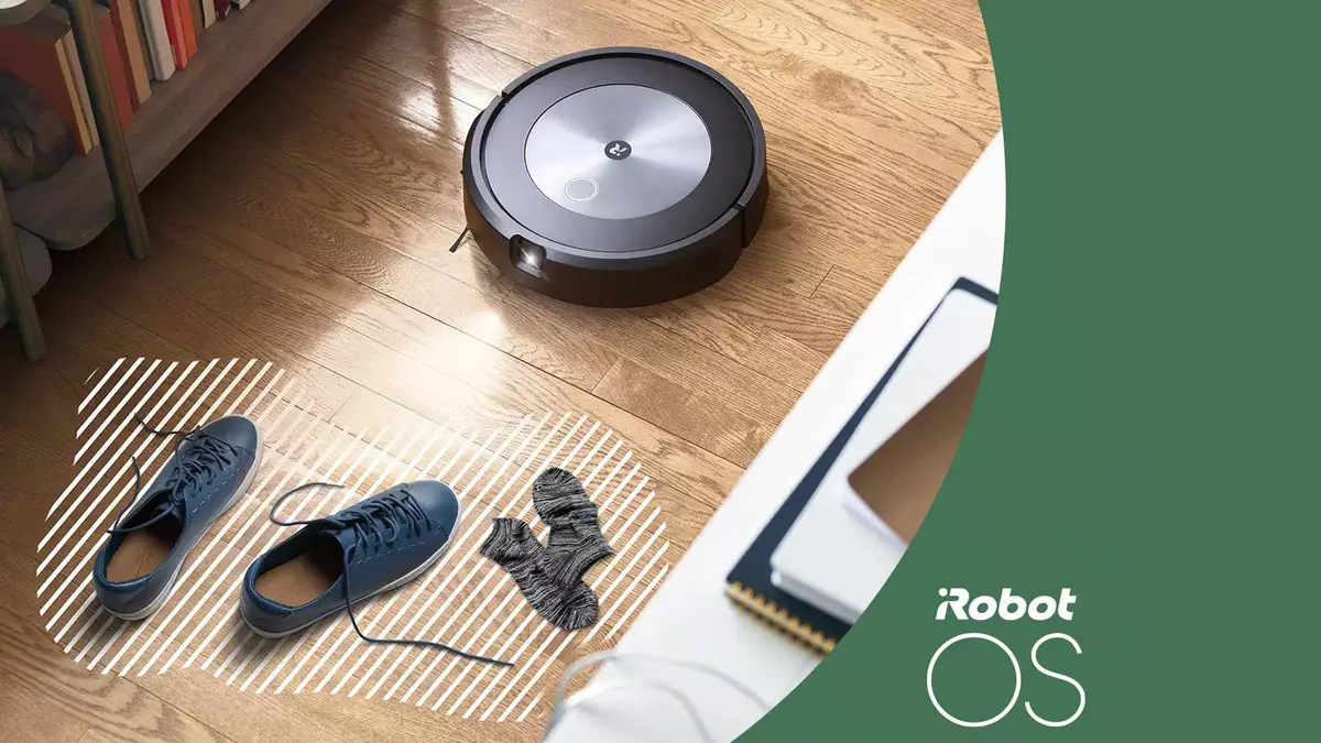 एक बुकशेल्फ़, जूते और मोजे के बगल में लकड़ी के फर्श पर एक iRobot वैक्यूम क्लीनर