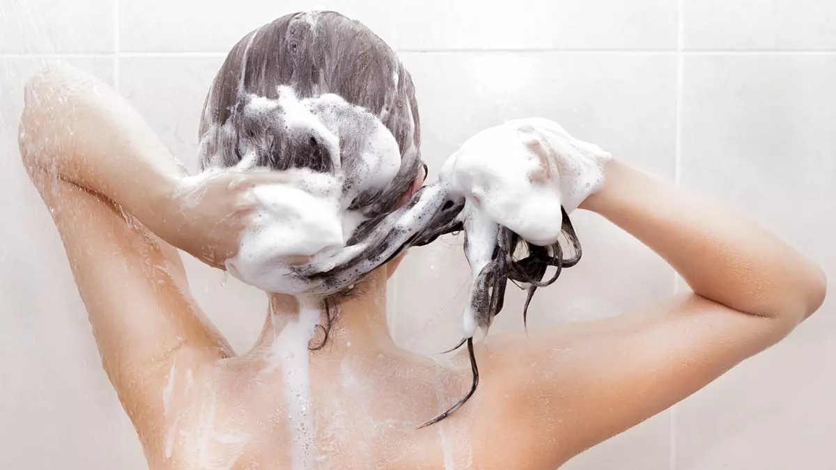 Մի կին ցնցուղի մեջ լվանում է իր մազերը.