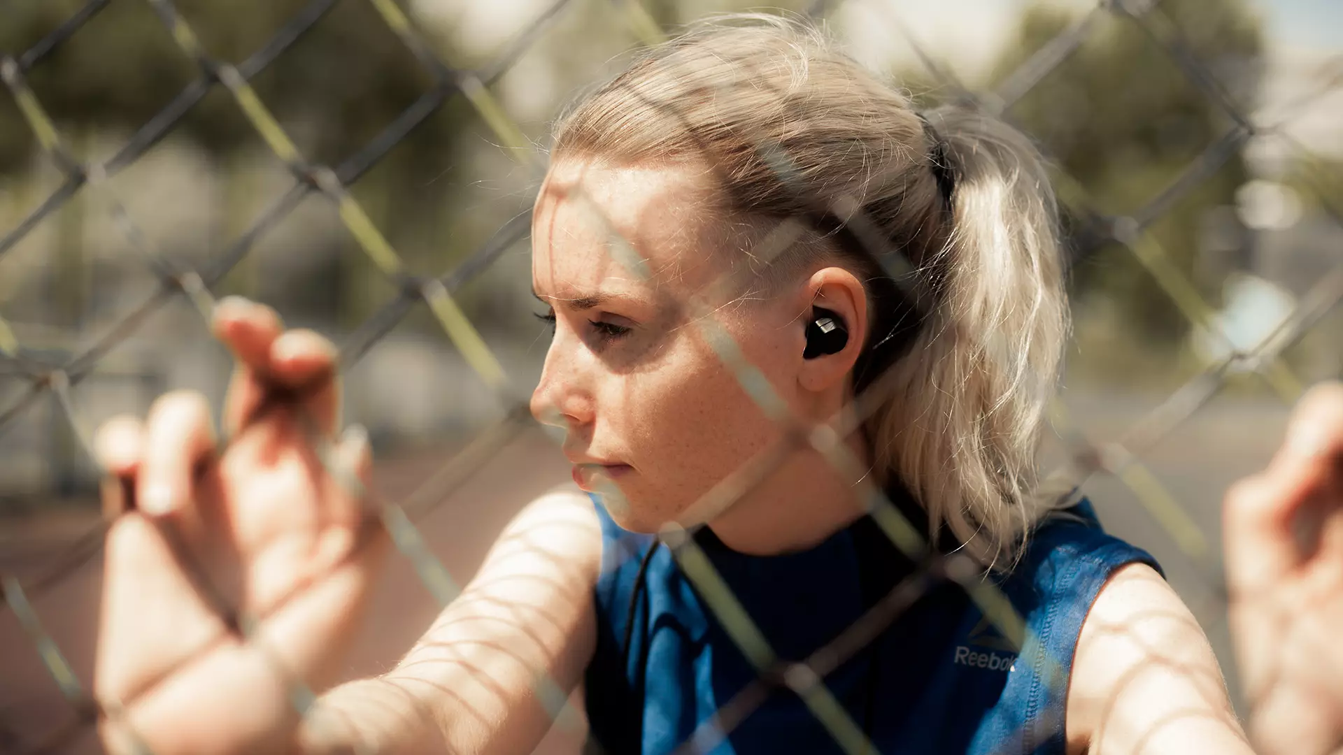 무선 이어폰을 귀에 꽂고 울타리에 기대어 있는 여성.