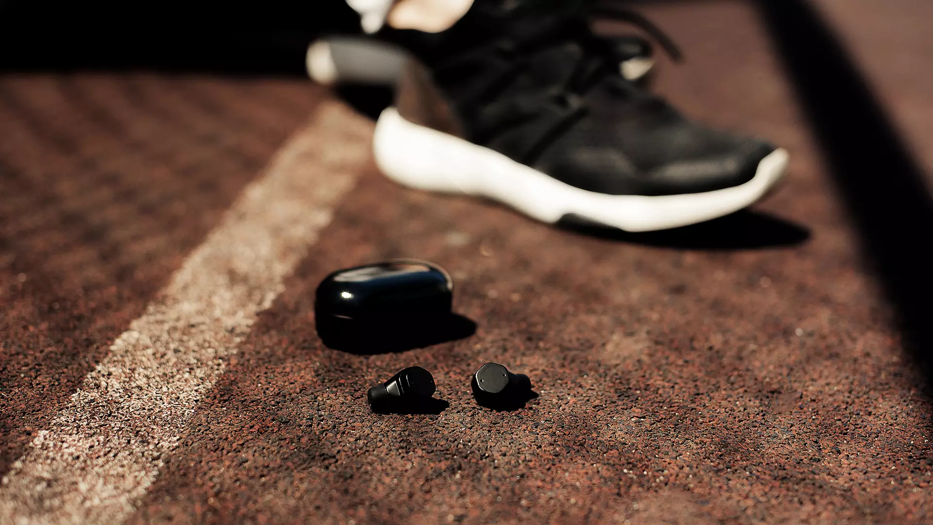 Мъжки крак в маратонка на бетонно спортно игрище до чифт безжични слушалки и калъфа им.