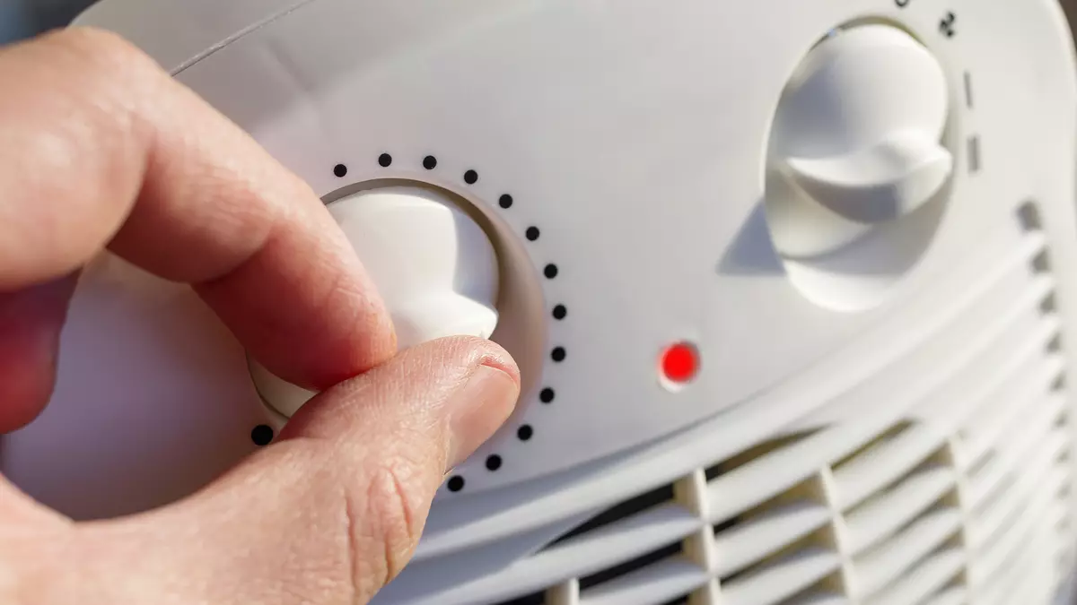 La main d'un homme tournant un bouton sur un radiateur d'appoint.