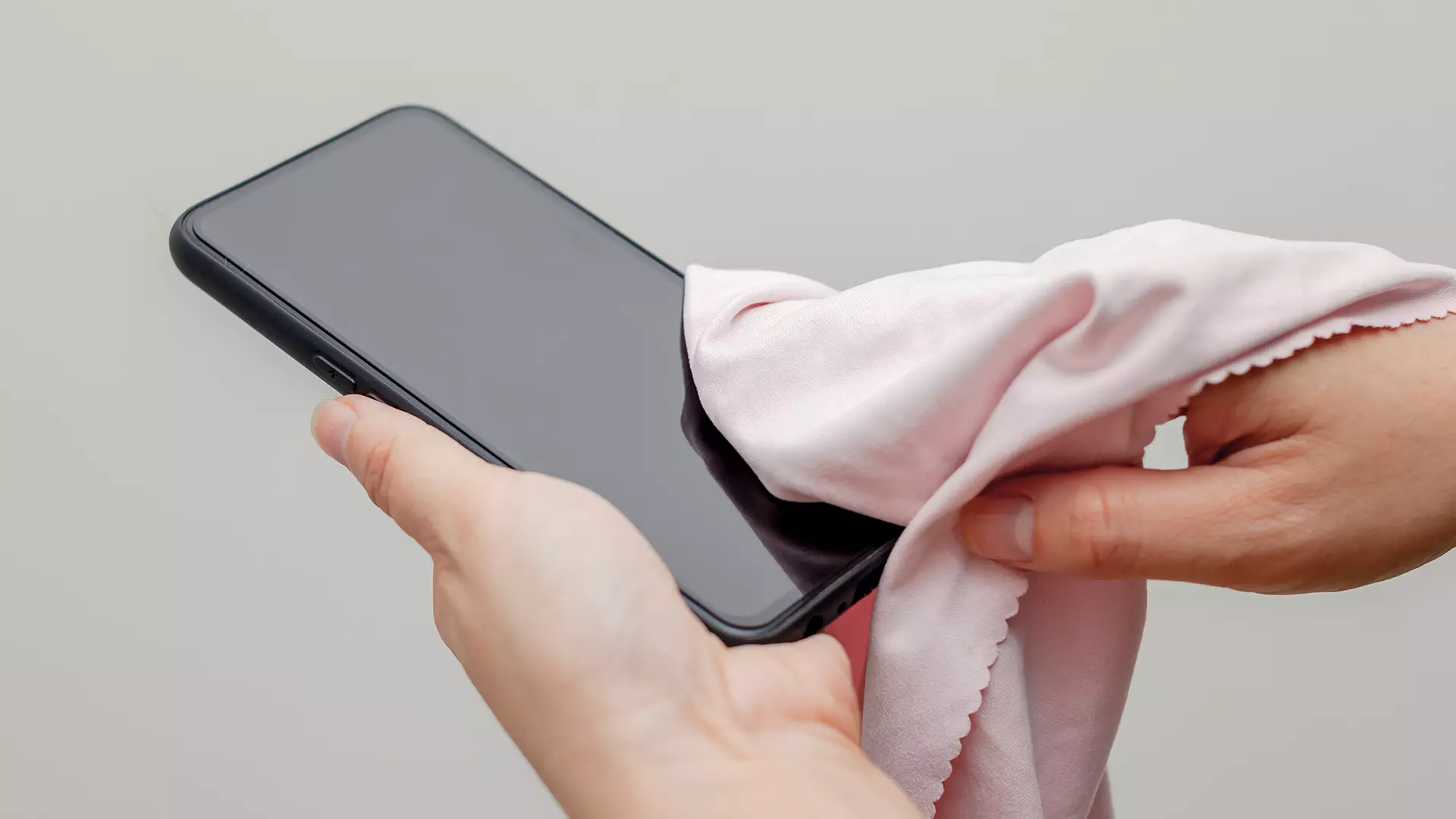 Foto seseorang membersihkan telepon dengan kain dan alkohol.
