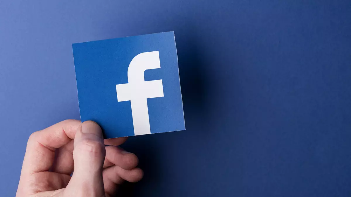Un recorte de papel do logotipo de Facebook diante dun fondo azul