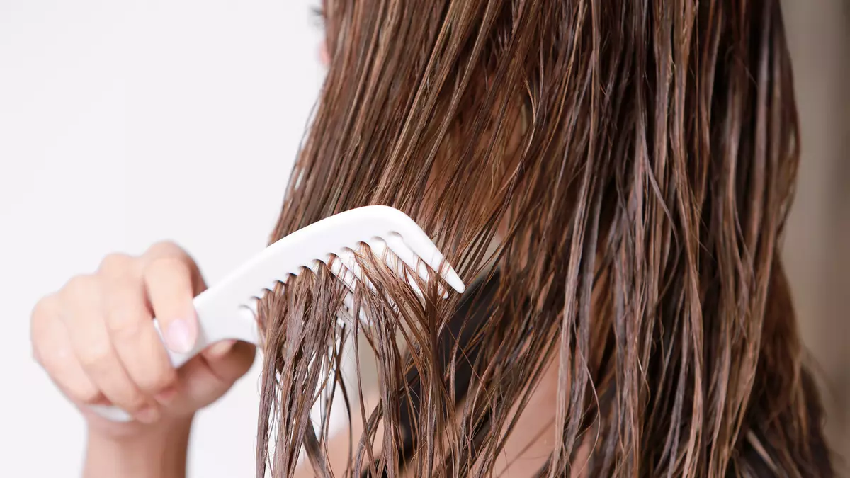 יד אישה מעבירה מסרק בשיער ארוך ורטוב.