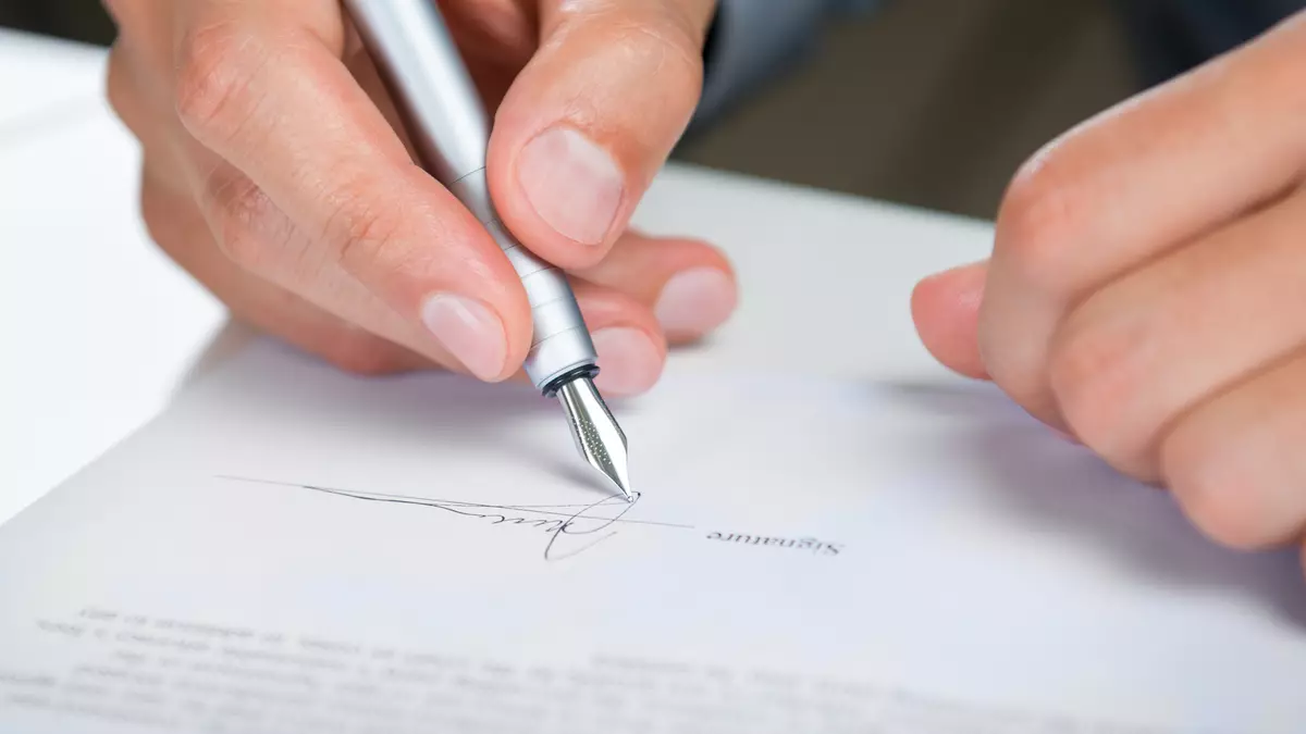Mâna unui bărbat care semnează un document cu un stilou.