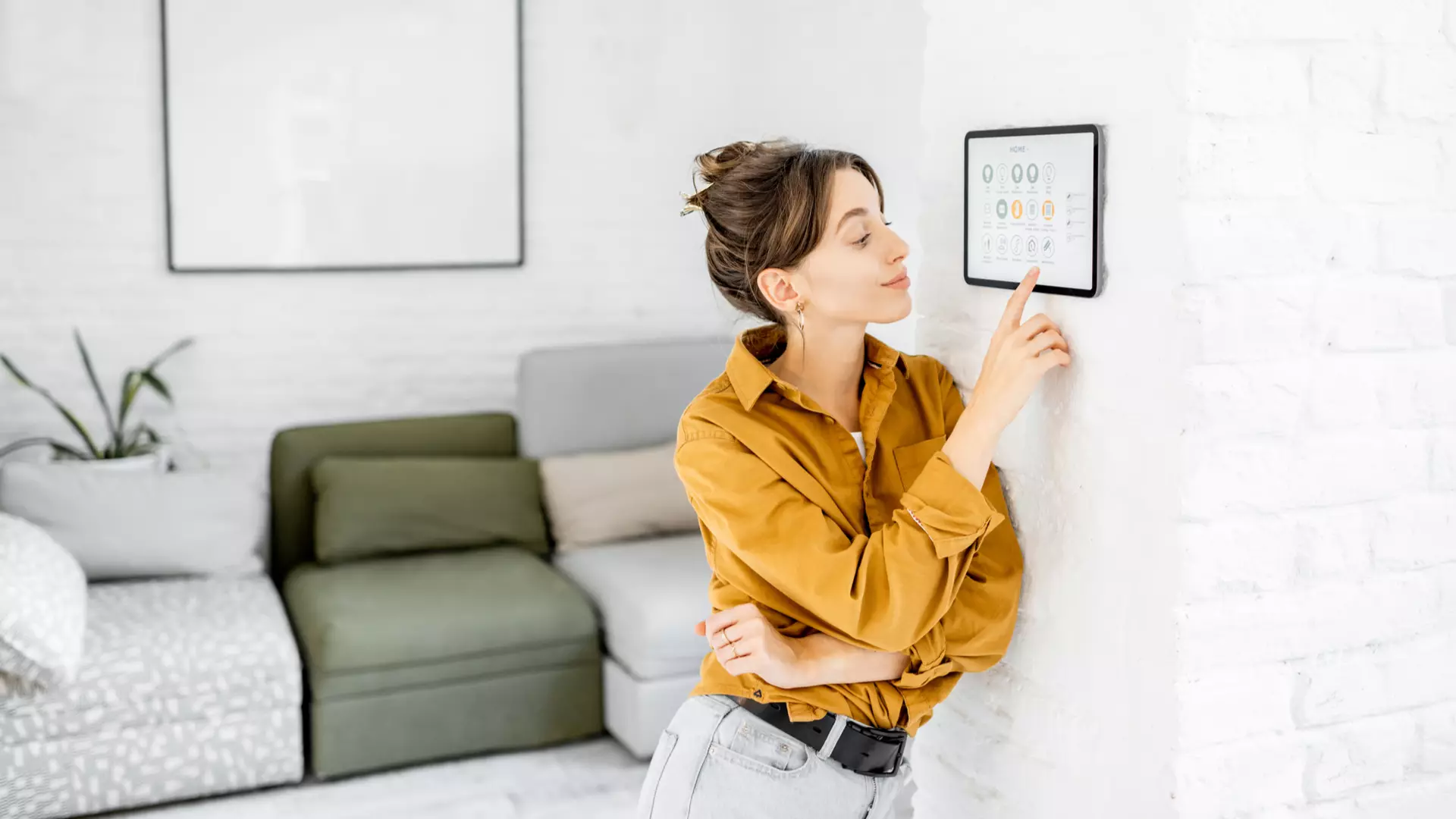 Persoană care controlează casa cu un panou digital tactil instalat pe peretele din camera de zi