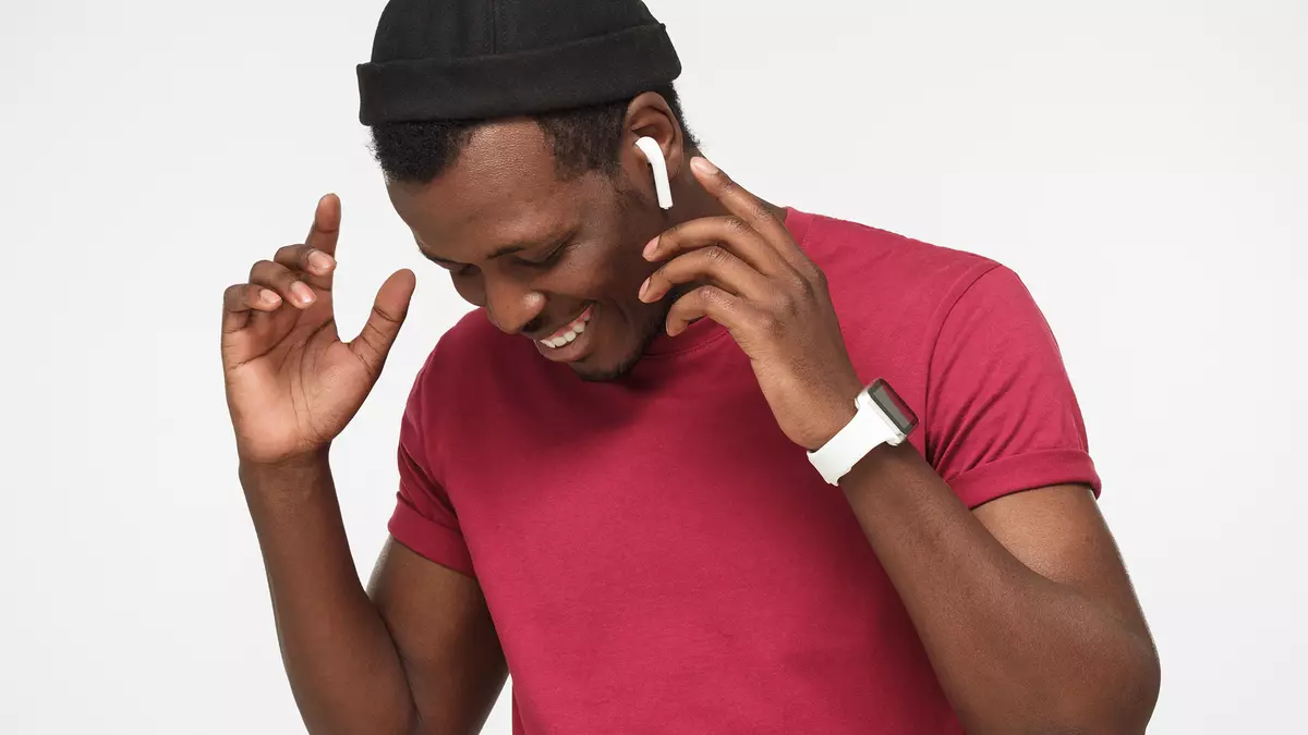 رجل يبتسم أثناء الاستماع إلى الموسيقى على سماعات أذنه اللاسلكية.