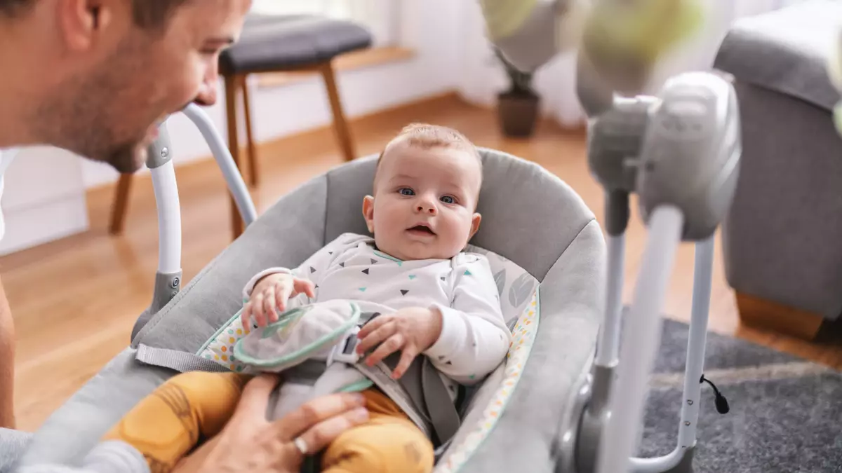 Gražus, rūpestingas jaunas baltaodžio tėvas žaidžia su savo žavingu 6 mėnesių sūnumi. Kūdikis guli kūdikio supamojoje kėdutėje ir jaučiasi patenkintas.