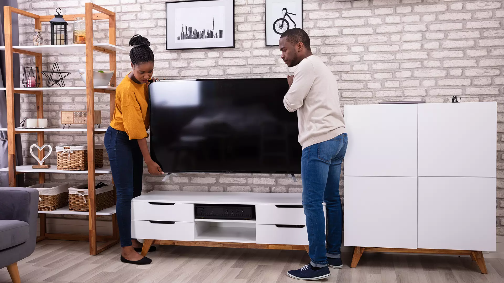 Jauns pāris savā mājā uzstāda jaunu televizoru.