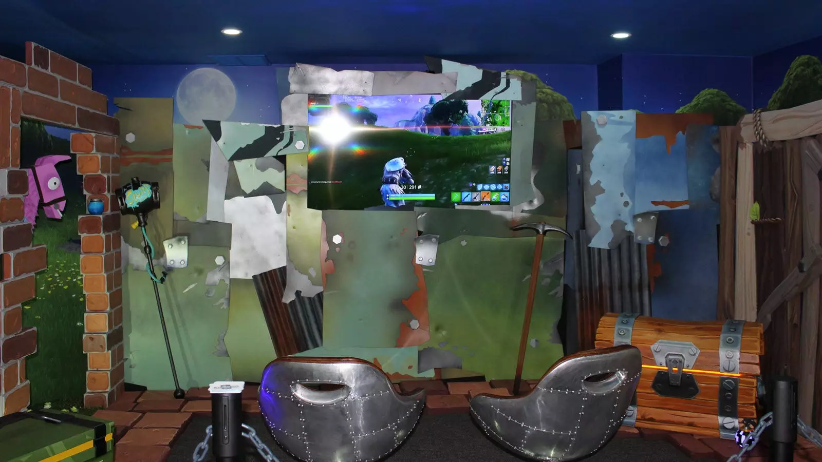 Isang game room na nagtatampok ng mga metal chair, treasure chest, at life-sized na in-game na item mula sa Fortnite.