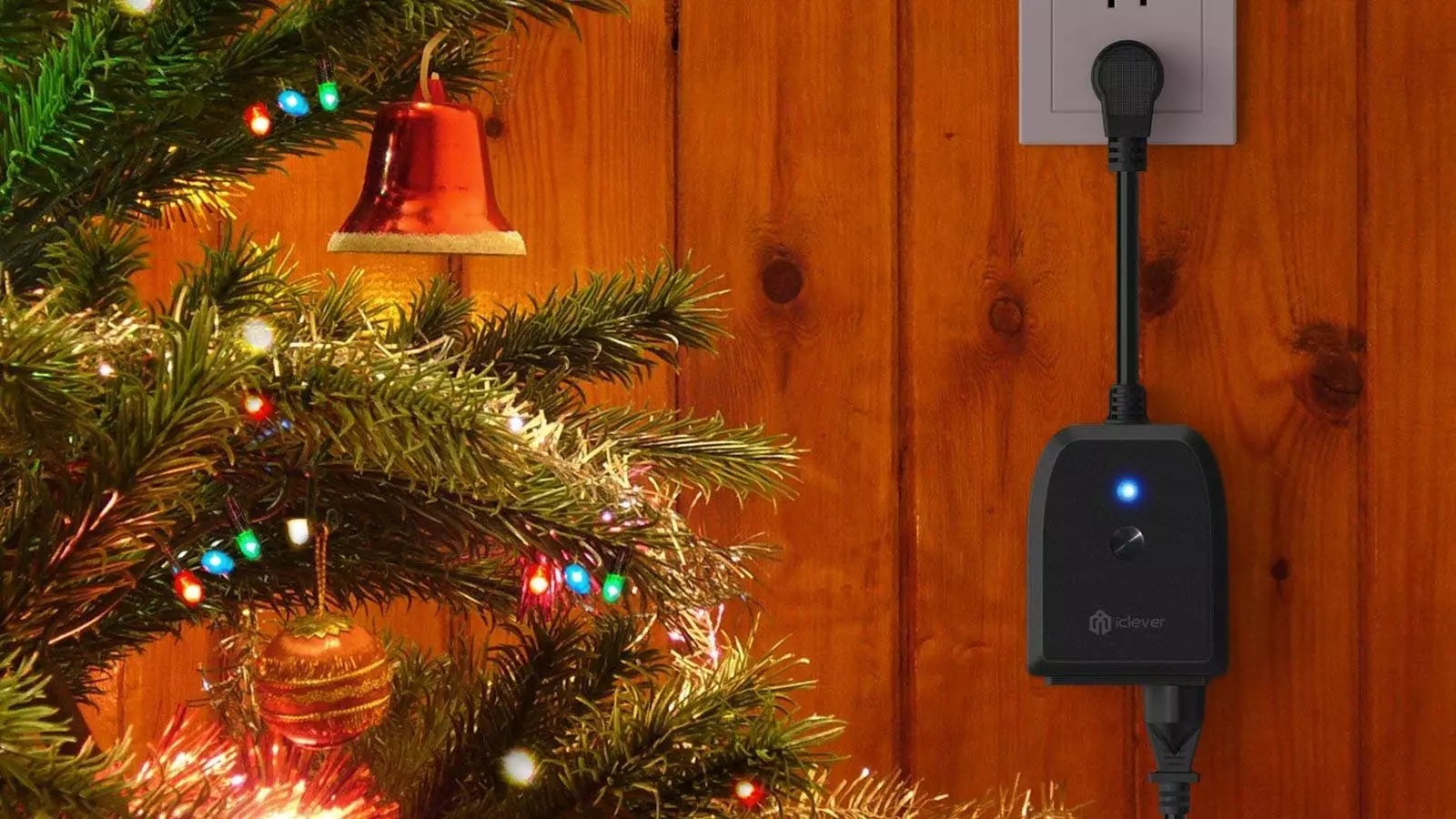 O priză inteligentă iClever conectată la perete de lângă un pom de Crăciun luminat.