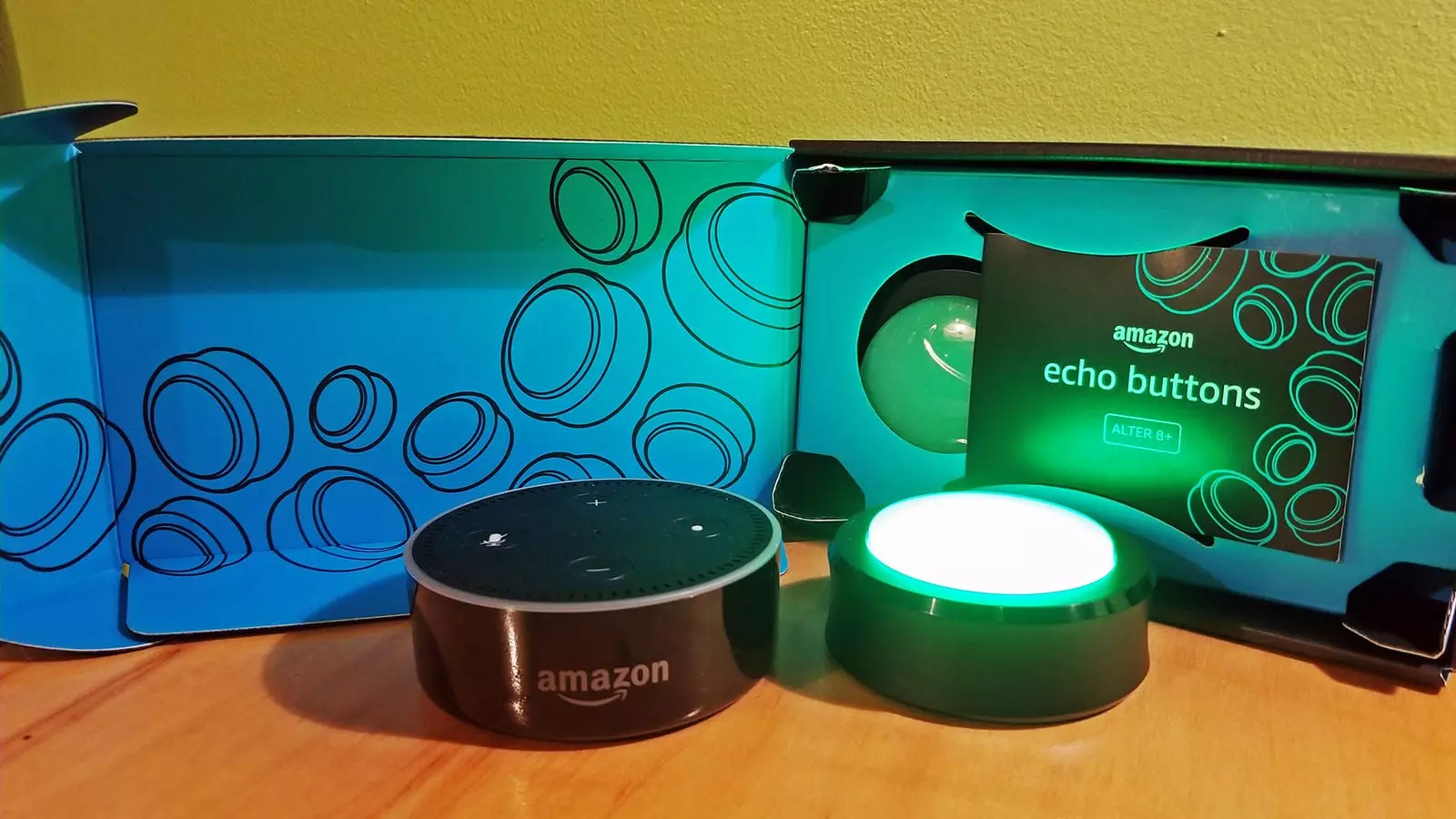 Amazon Echo û bişkokek Echo ya kesk a geş li ber qutiyên wan.
