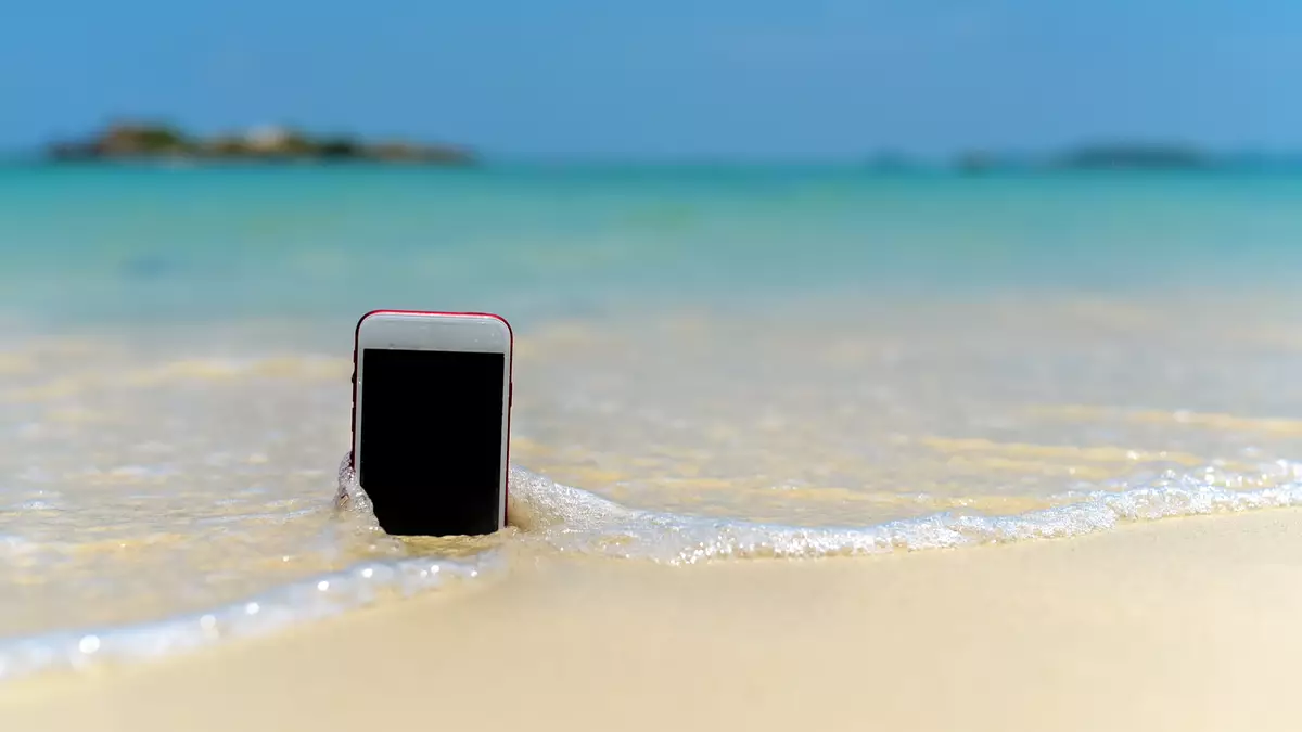 Смартфон застрял в песке со световыми волнами, разбивающимися о него