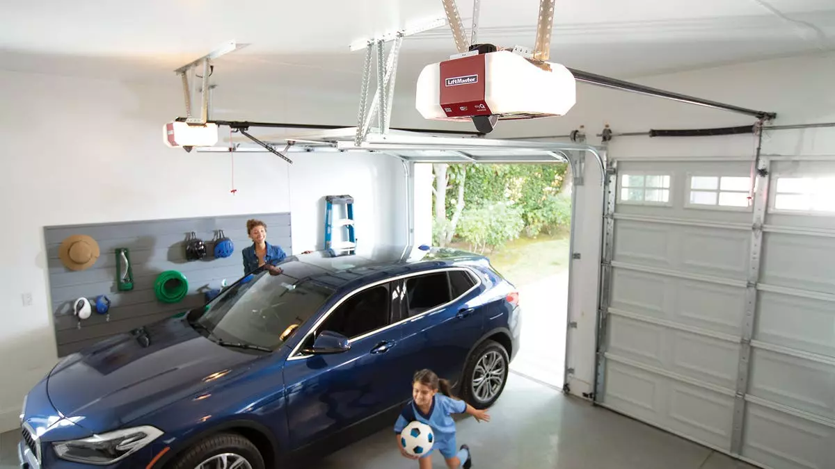 El abre-puertas de garaje WI-FI de LiftMaster con cámara integrada colgado en un garaje sobre una niña con una pelota de fútbol.