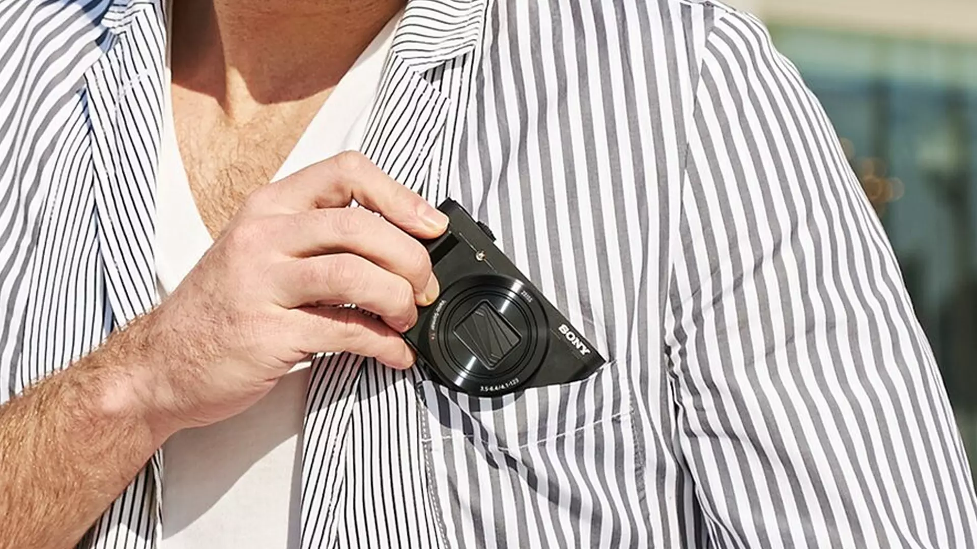 En mann stikker et kompaktkamera fra Sony i lommen.