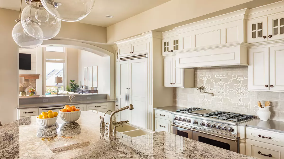 Eine moderne, weiße Küche mit einem Edelstahlherd, zwei Bauernspülen und Granit-Arbeitsplatten in Marmoroptik.