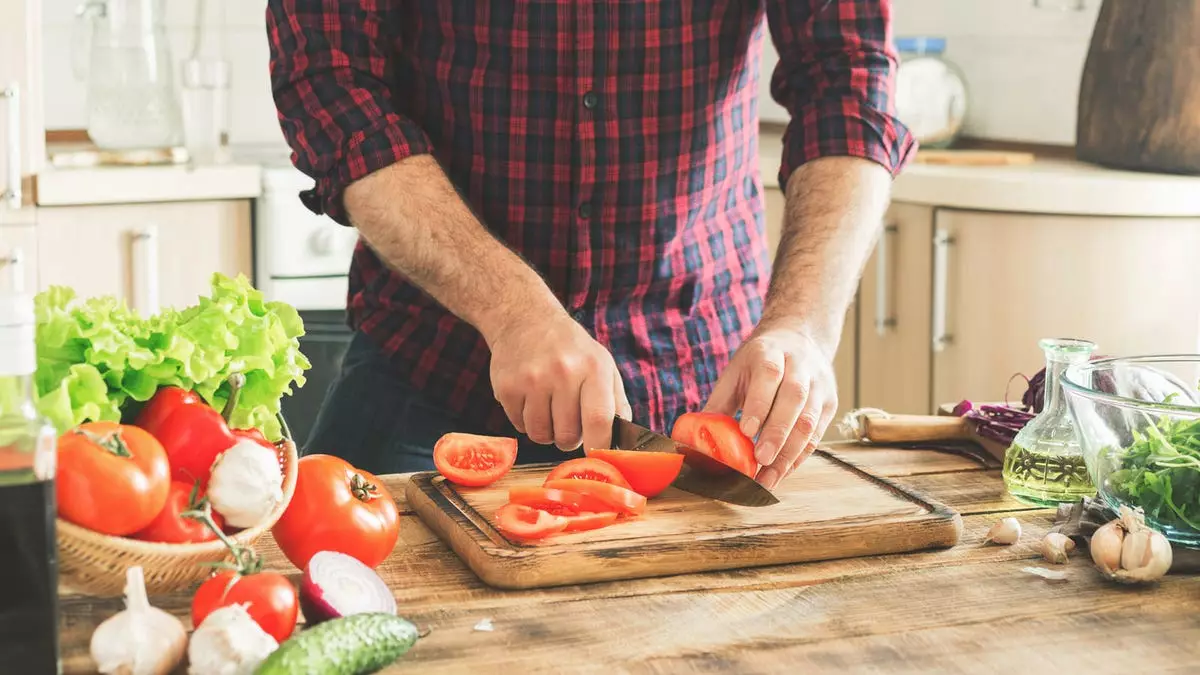 Un home cortando tomates nunha táboa de cortar con ranuras de zume nunha cociña.