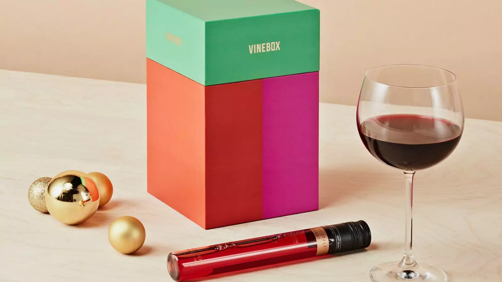 Unha Vinebox xunto a uns adornos de Nadal, unha copa de viño e un frasco cheo dunha mostra de viño.